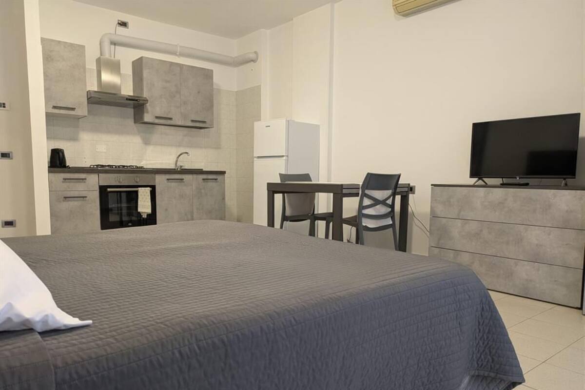 Quarto de hotel moderno com uma cama grande, cozinha compacta, área de refeições e televisão.
