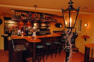 Uma área de bar com balcão de madeira, banquetas e diversos frascos e copos.
