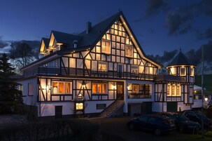 Uma grande casa em estilo Tudor, com dois andares, uma torre saliente e uma entrada bem iluminada.