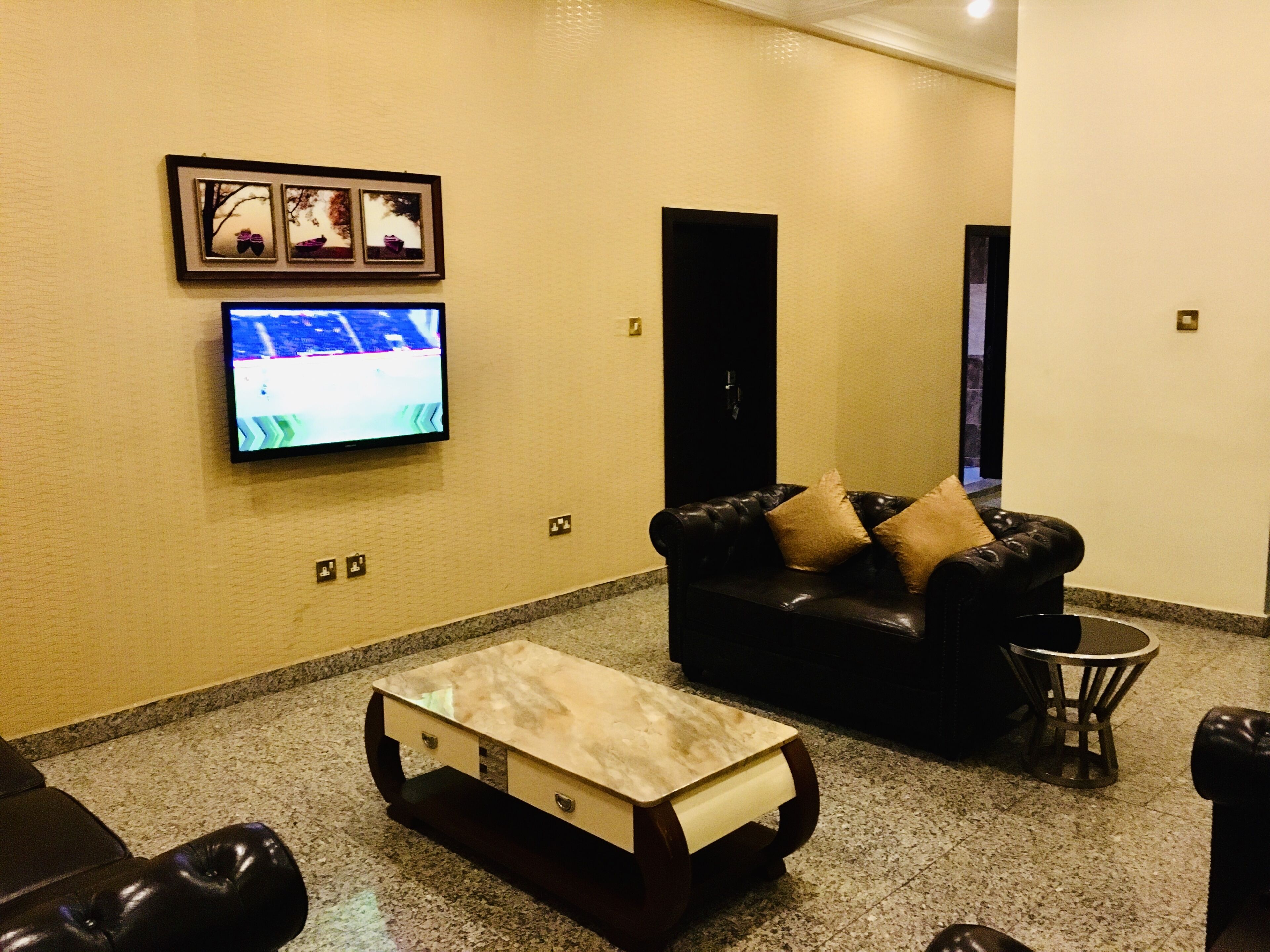 Um hall de hotel com um sofá de couro, uma mesa pequena, uma televisão e quadros nas paredes.