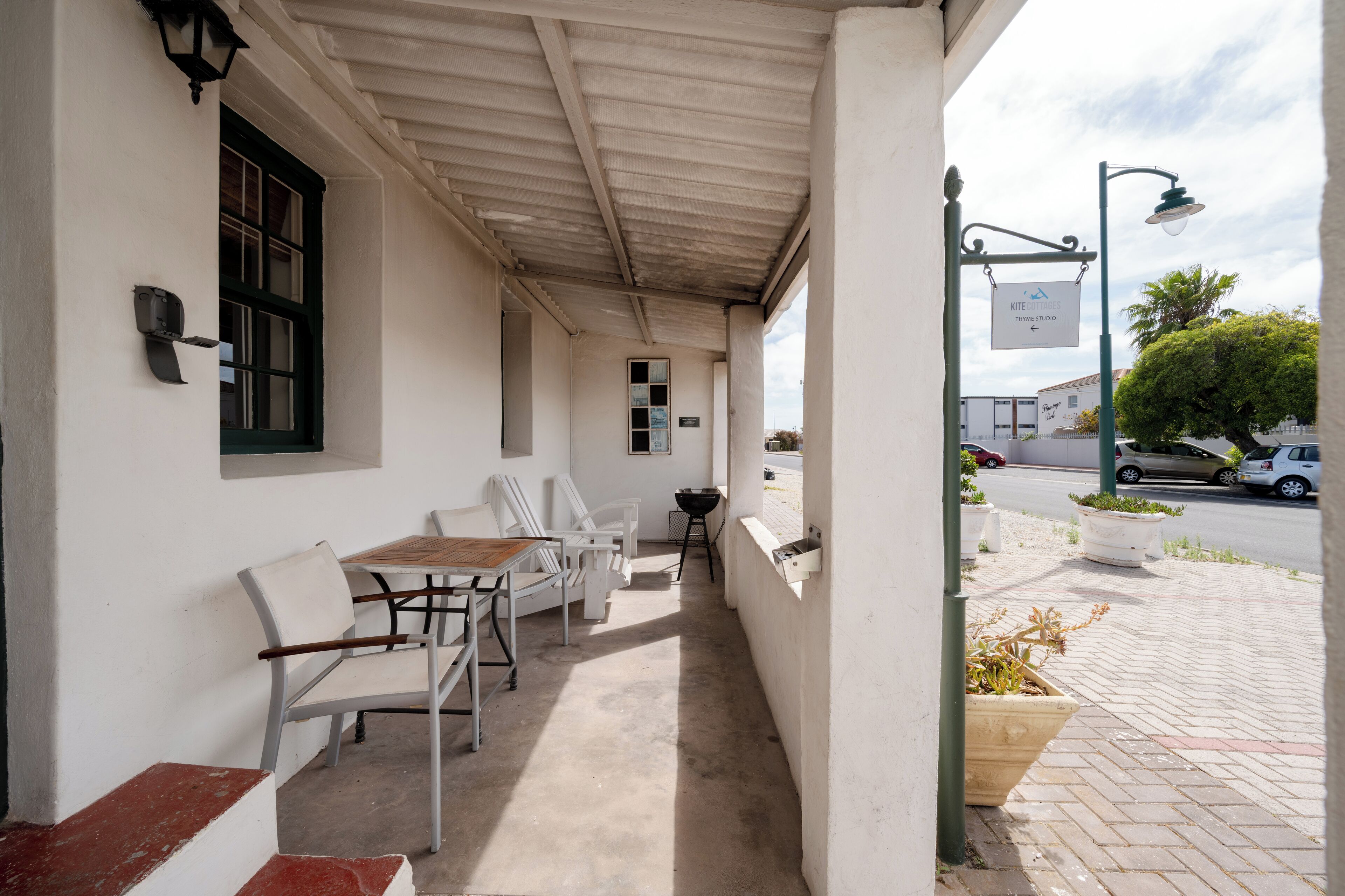 Uma área de estar coberta ao ar livre, com mesa, cadeiras, lixeira e uma placa com a inscrição 'Kite Studio'.