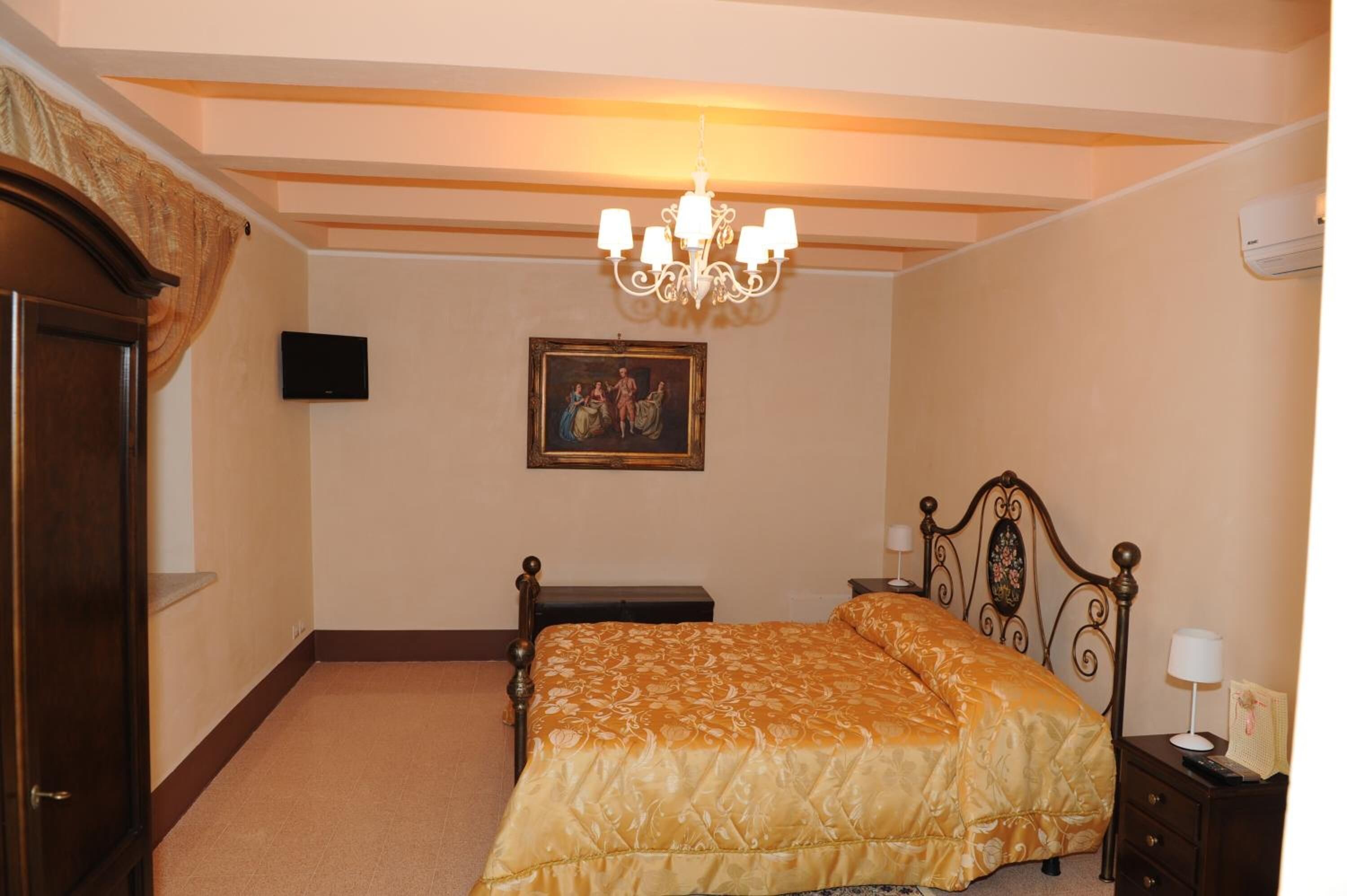 Quarto com cama, lustre, pintura, televisão e mesa de cabeceira.