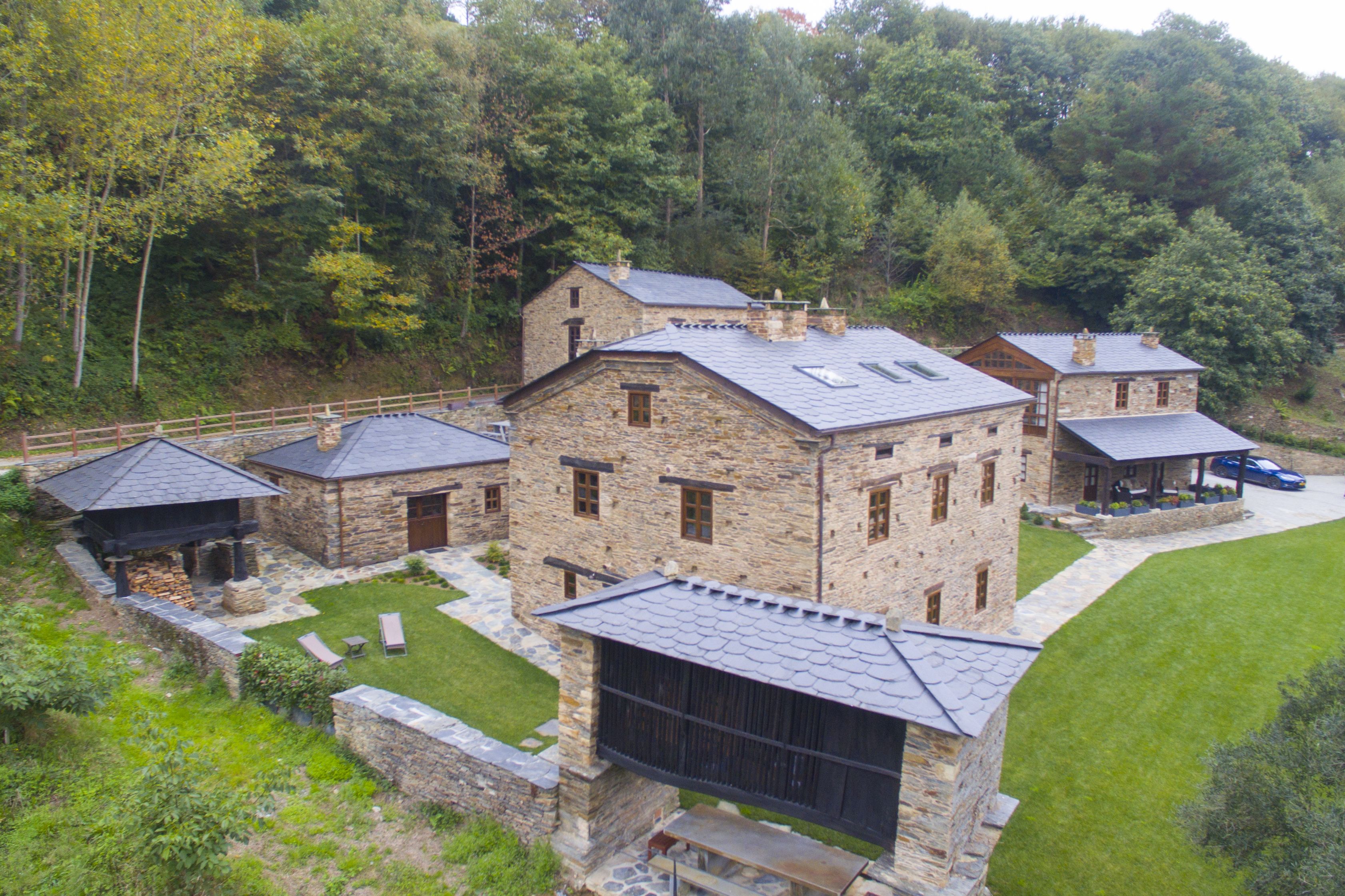 Um edifício de pedra com vários quartos, área externa coberta e gramado bem cuidado.
