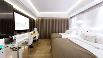 Quarto de hotel moderno com televisão de tela plana, escrivaninha com cafeteira, cadeira, cama com roupa de cama branca e uma grande janela com cortinas.