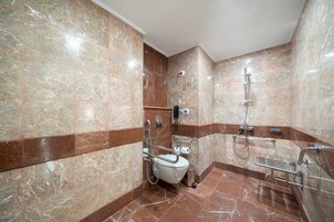 Um banheiro com piso de mármore, vaso sanitário branco, chuveiro e corrimão.