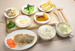 Uma mesa de madeira com diversos pratos, incluindo peixe, arroz, sopa e legumes.
