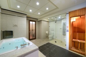 Um banheiro moderno com banheira, box de vidro e área de sauna em madeira.