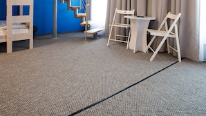 Quarto com parede azul, escada de madeira, mesa branca e uma grande janela com cortinas.