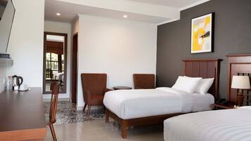 Quarto de hotel com cama, duas cadeiras, escrivaninha, cafeteira e um quadro na parede.