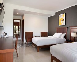 Quarto de hotel com cama, duas cadeiras, escrivaninha, cafeteira e um quadro na parede.