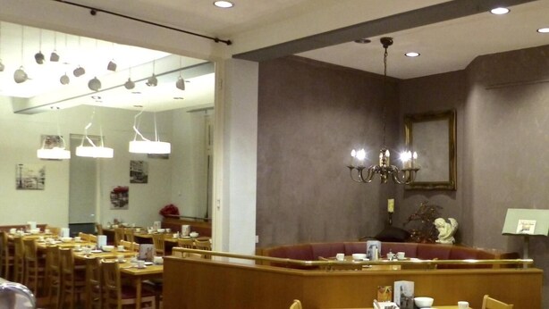 Um restaurante com mesas e cadeiras de madeira, área de bar e um lustre.