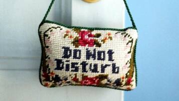 Uma porta com uma pequena placa bordada que diz “Não Perturbe” e uma fechadura.