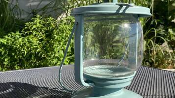 Um lanterna azul transparente sobre uma mesa de metal ao ar livre, com vegetação ao fundo.