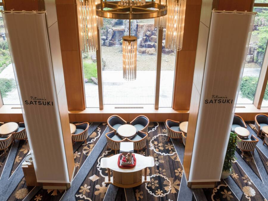 Interior moderno com área de estar central, um candelabro e vista para uma paisagem natural através de amplas janelas.