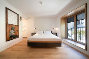 Quarto moderno com cama grande, piso de madeira, janela ampla e obras de arte na parede.