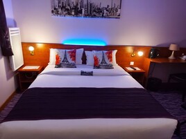 Quarto de hotel com uma cama, duas mesas de cabeceira, um criado-mudo, uma lâmpada e um quadro na parede.