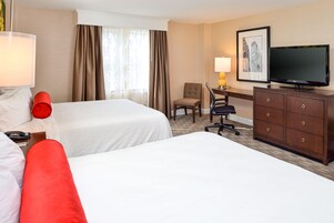 Quarto de hotel com duas camas, uma escrivaninha com cadeira, televisão e cómoda.