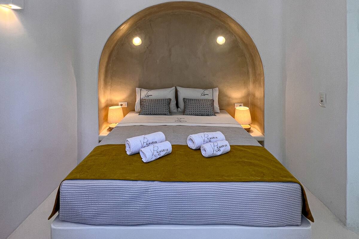 Quarto moderno com uma cama grande, duas luminárias de cabeceira e um teto em arco distinto.