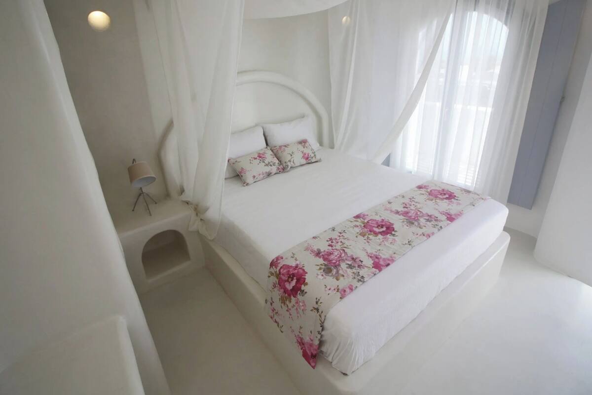 Quarto com cama de dossel, mesa de cabeceira e um banquinho.