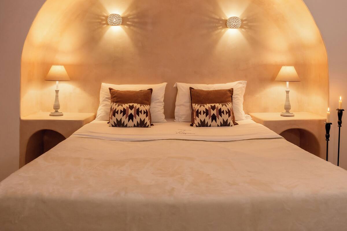 Quarto com uma cama grande, duas luminárias de cabeceira e cabeceira com iluminação integrada.