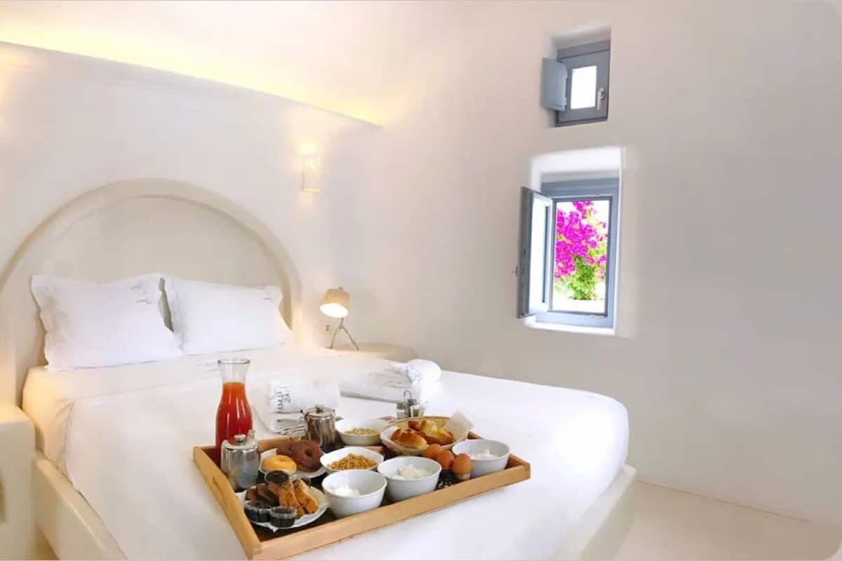 Cama bem arrumada com uma bandeja de itens de café da manhã, abajur e janela com vista para flores.