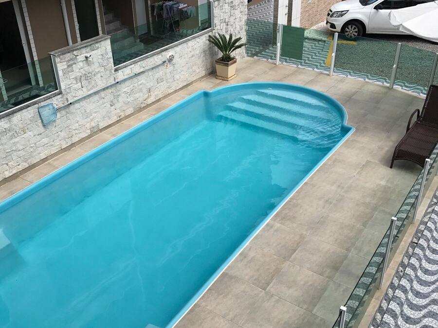 Piscina retangular com deck ladrilhado, cercada por um pequeno muro.
