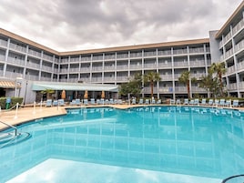 Um hotel com uma piscina grande, várias varandas e uma área de estar coberta.