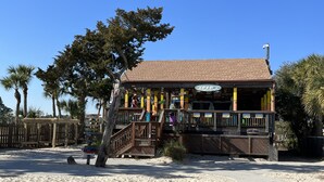 Um edifício à beira-mar com telhado em telhas, deck de madeira e detalhes verticais coloridos.