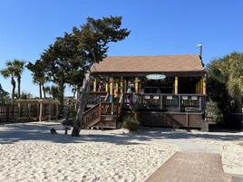 Um edifício à beira-mar com telhado em telhas, deck de madeira e detalhes verticais coloridos.