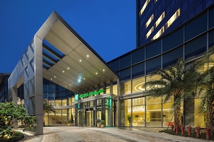Entrada moderna de um hotel com galeria coberta, portas de vidro e placa indicando Holiday Inn.