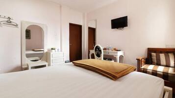 Quarto de hotel com cama, escrivaninha, cadeira, televisão na parede e janela.