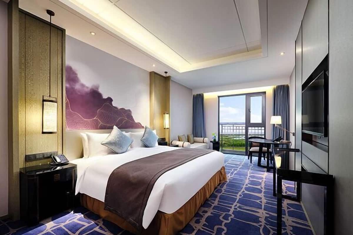 Quarto de hotel com uma cama grande, uma escrivaninha, televisão e varanda com vista.