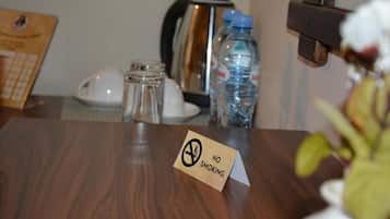 Quarto de hotel com uma mesa de madeira, placa de proibido fumar, garrafa de água, cafeteira e telefone.