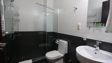 Casa de banho com chuveiro em cabine de vidro, sanita branca e lavatório.