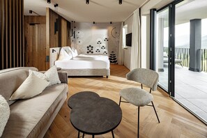 Quarto moderno com cama, sofá e cadeiras, parede de madeira e uma janela grande.