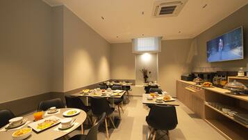 Uma sala de jantar moderna com várias mesas e cadeiras, um balcão de buffet e uma televisão exibindo um programa.