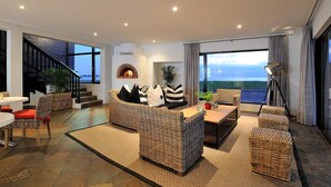 Uma sala de estar ampla com móveis de vime, lareira e vista para o mar.