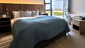 Quarto com uma cama grande, uma escrivaninha e vista para a praia.