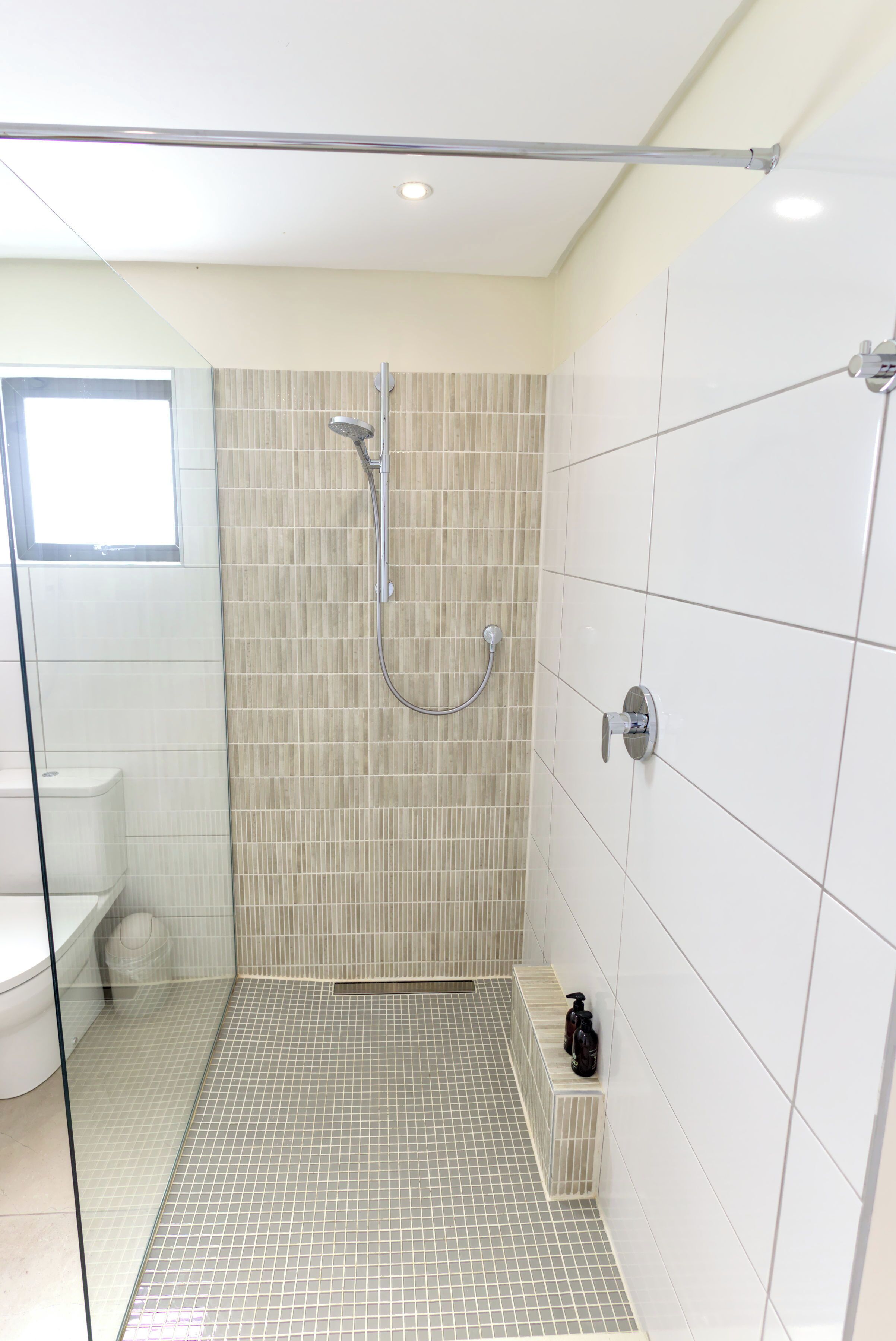 Um chuveiro moderno com porta de vidro, paredes revestidas de azulejos e um banco embutido.