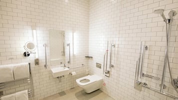 Casa de banho moderna com azulejos brancos tipo metrô, sanita branca, lavatório, espelho e chuveiro com porta de vidro.