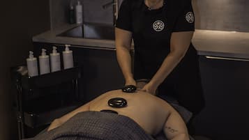 Sessão de massagem em um quarto com pouca luz, com uma mesa de massagem, pia e prateleira com frascos.