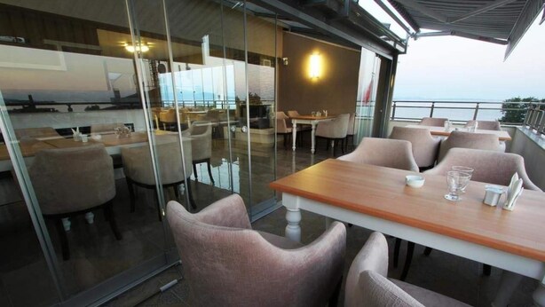 Restaurante com paredes de vidro, oferecendo vista para o mar. Mesas e cadeiras dispostas para refeições.
