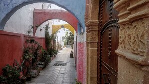 Uma viela estreita com uma porta de madeira e uma parede vermelha e branca.