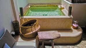 Uma área de spa com uma banheira, um cesto de vime, um pequeno banquinho e uma vela.