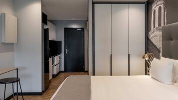 Quarto de hotel moderno com cama, escrivaninha, cadeira, televisão e guarda-roupa.