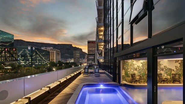 Área de piscina no terraço com hidromassagem, espreguiçadeiras e vista para a cidade ao entardecer.