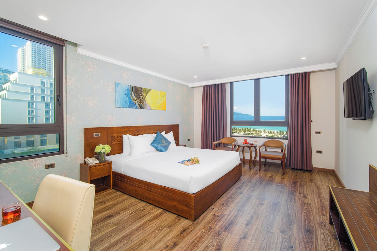 Quarto de hotel com uma cama grande, uma escrivaninha, uma cadeira, uma televisão e uma janela com vista para a cidade.