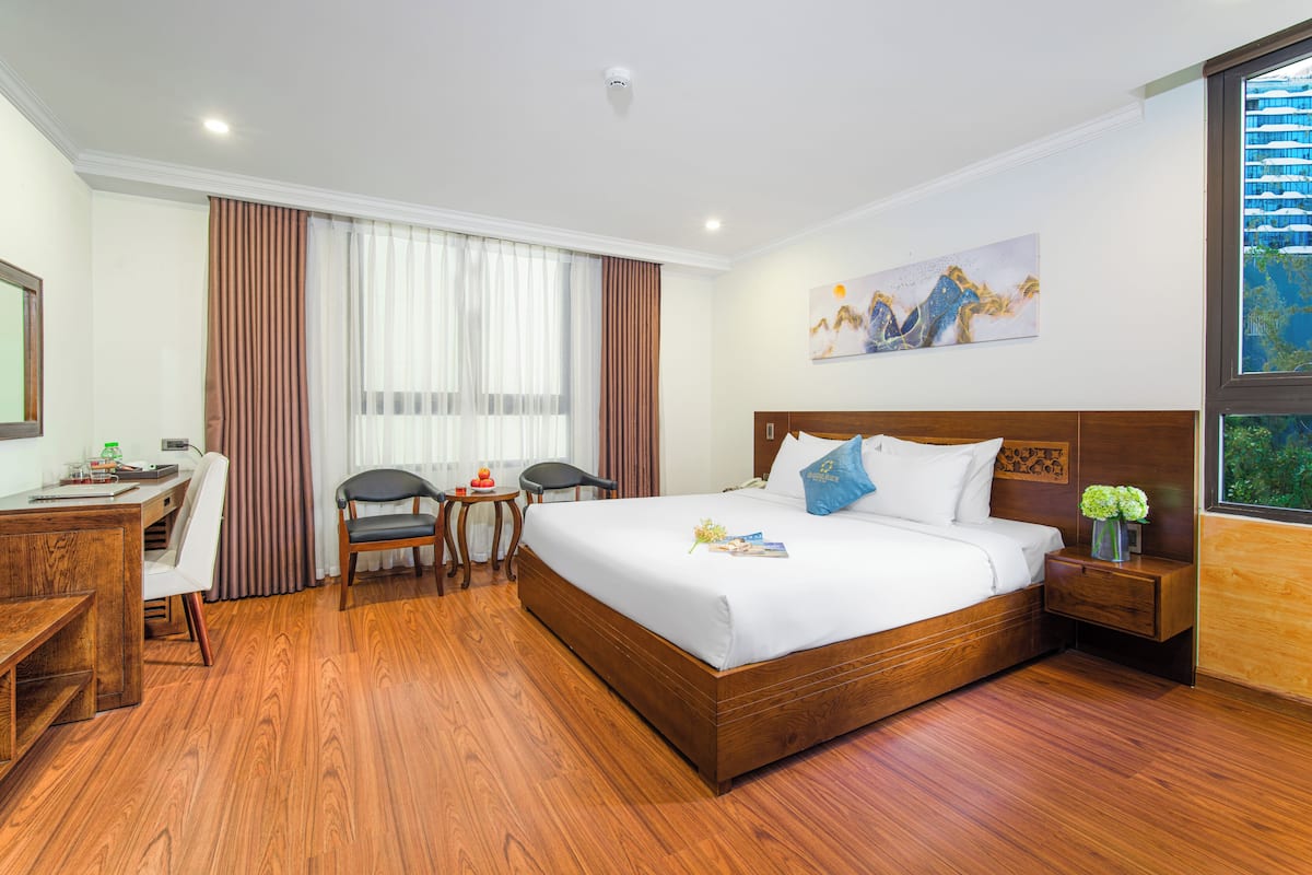 Quarto de hotel com cama de madeira, escrivaninha, cadeira e janela com cortinas.