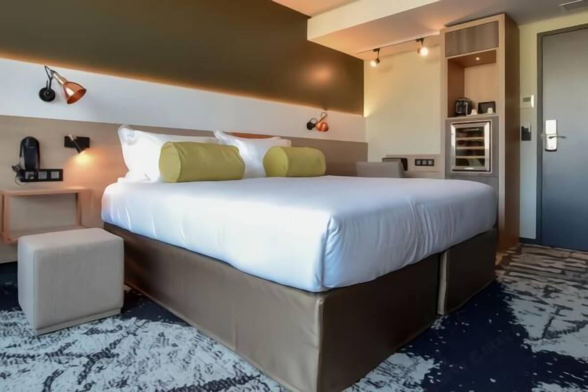 Quarto de hotel moderno com uma cama grande, mesas de cabeceira, um pequeno espaço de estar e um guarda-roupa embutido.
