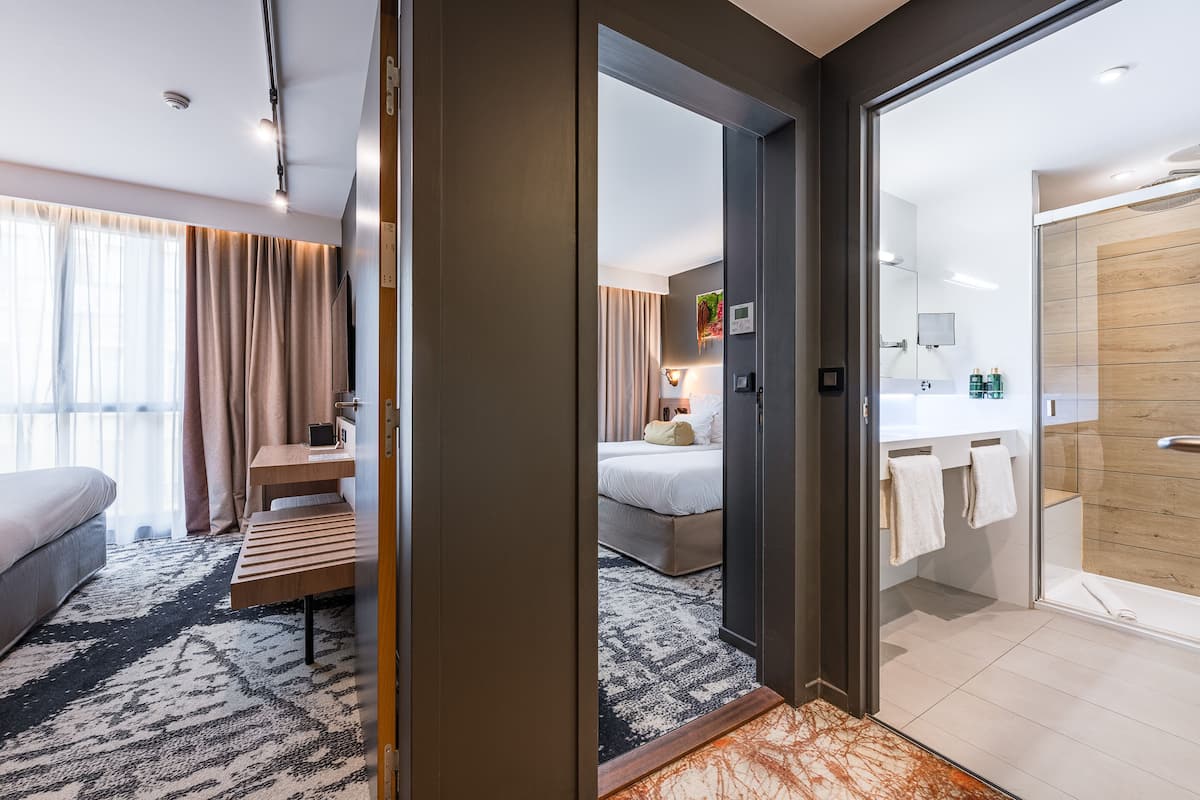 Quarto de hotel moderno com cama, mesa de cabeceira e um espelho grande.